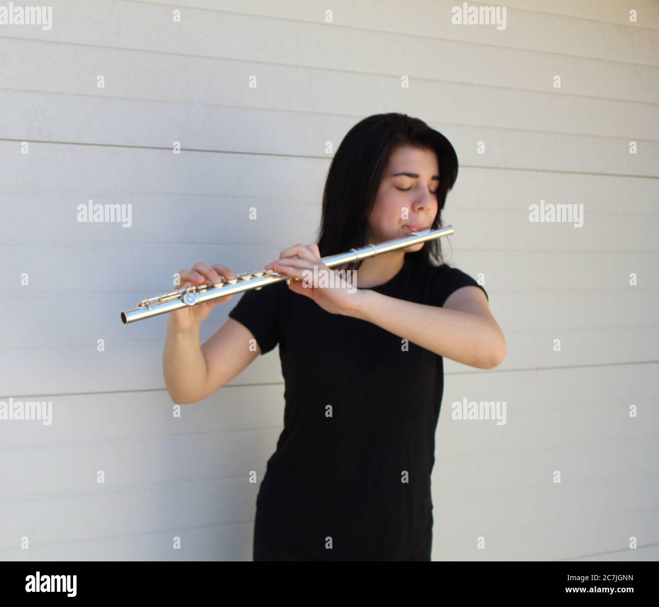 Black-haired girl plays the flute outside in front of a white ...