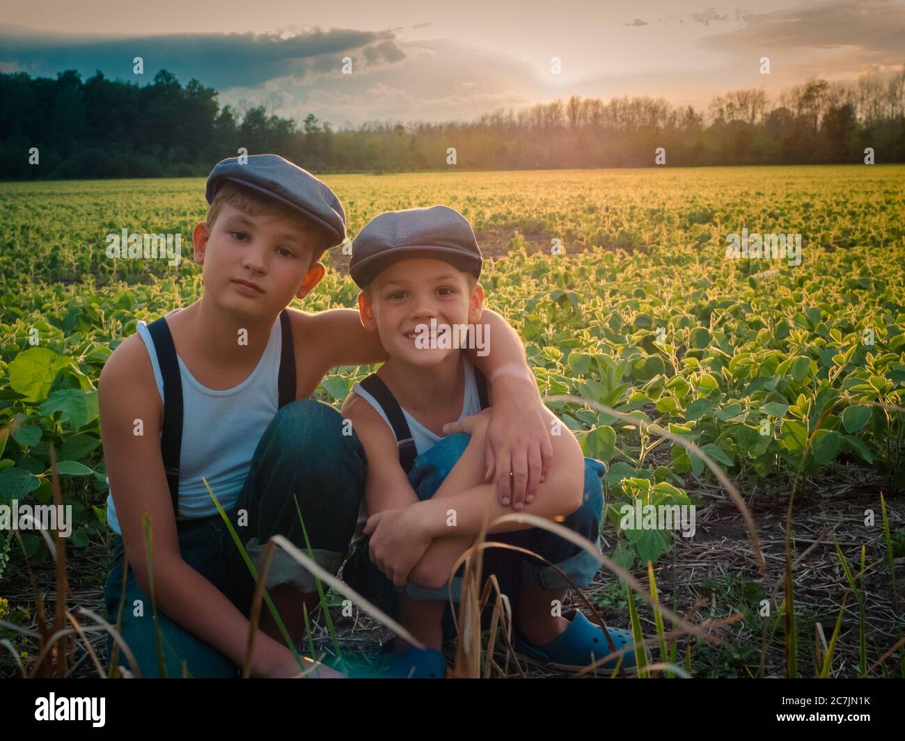 Brothers with hats and suspenders in a field covered in greenery during ...