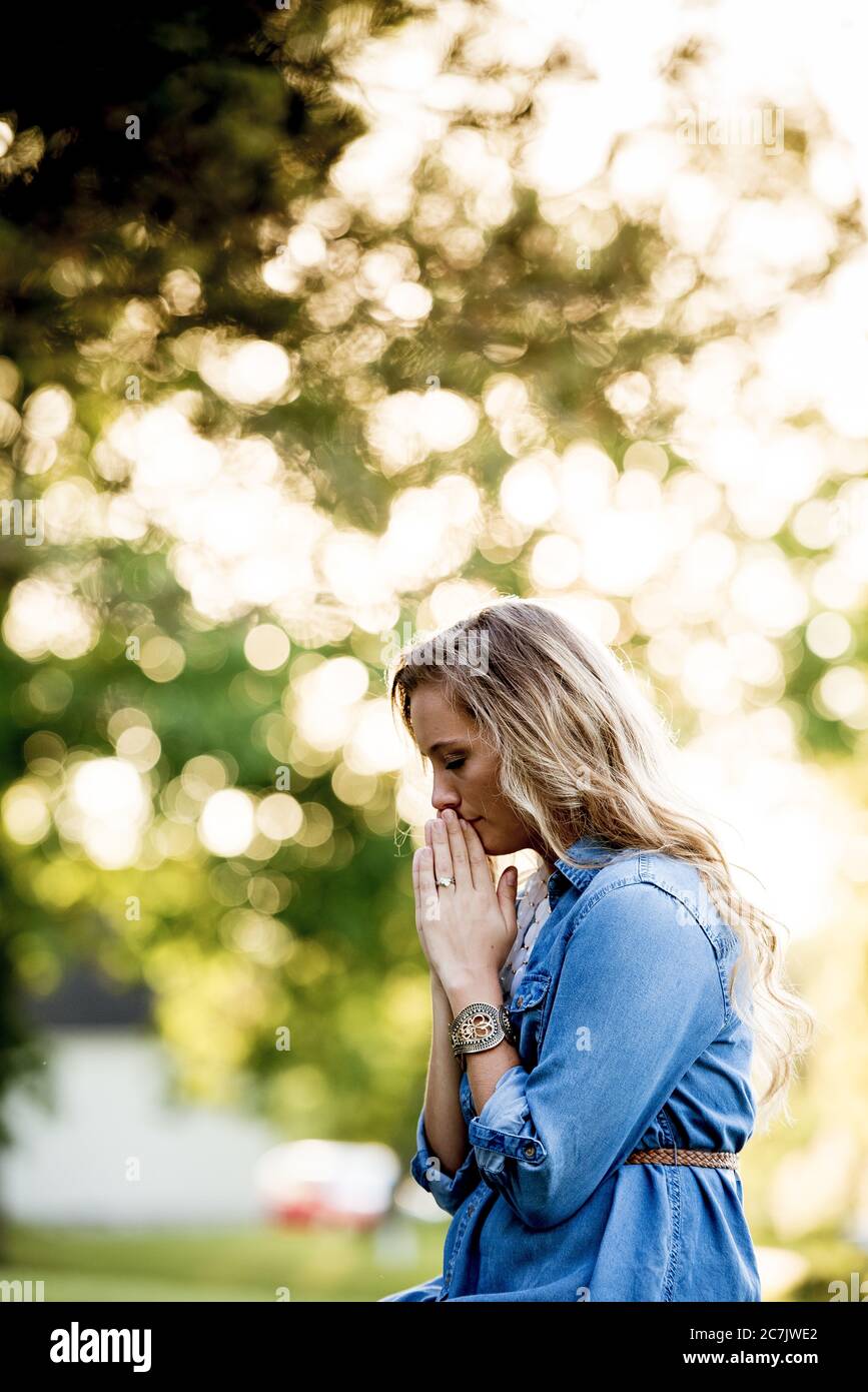 Woman wearing a blue dress and praying in a garden under sunlight with ...