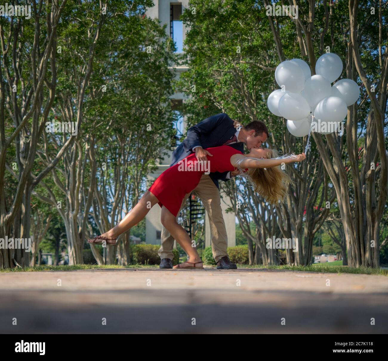 Kissing couple with balloons in a garden surrounded by trees under the ...