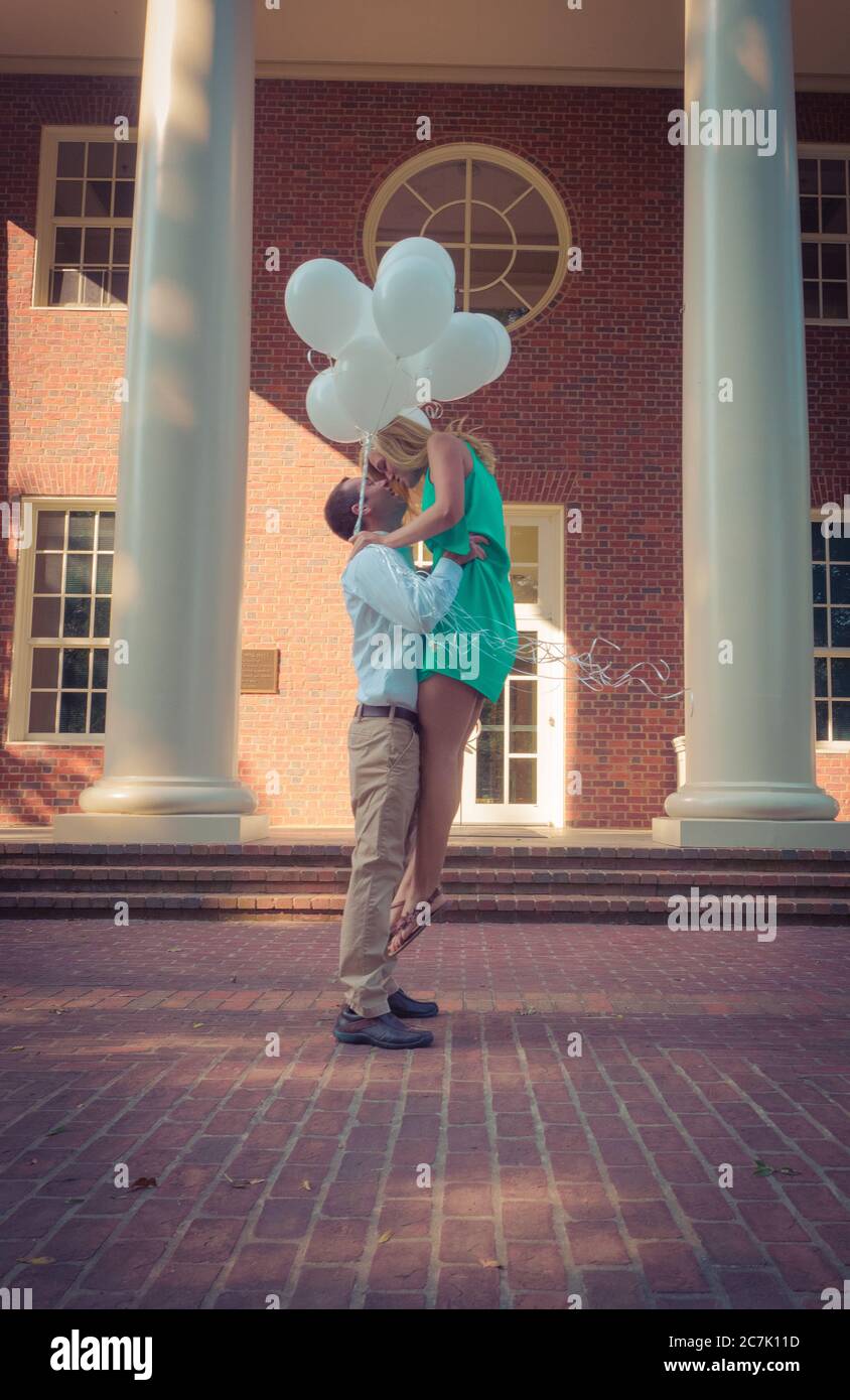Couple holding balloons hugging and kissing in front of a building ...