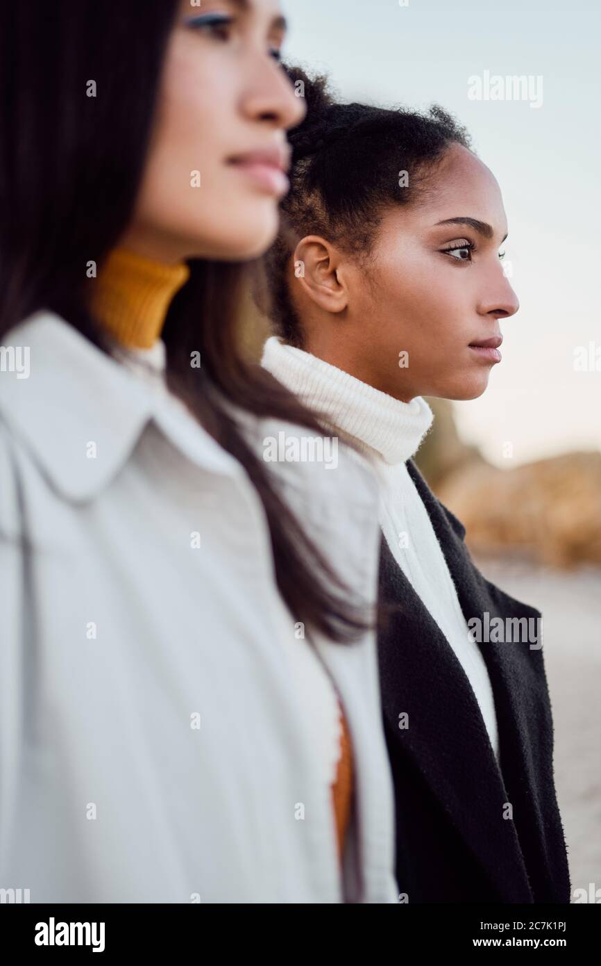 Close up two attractive girls in trench coats dreamily standing ...