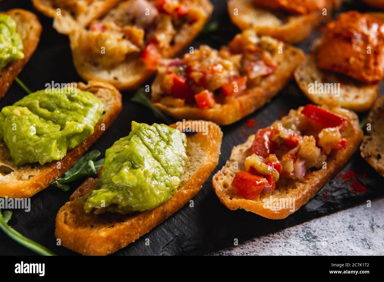 Assorted bruschetta with various toppings on a dark plate on white ...