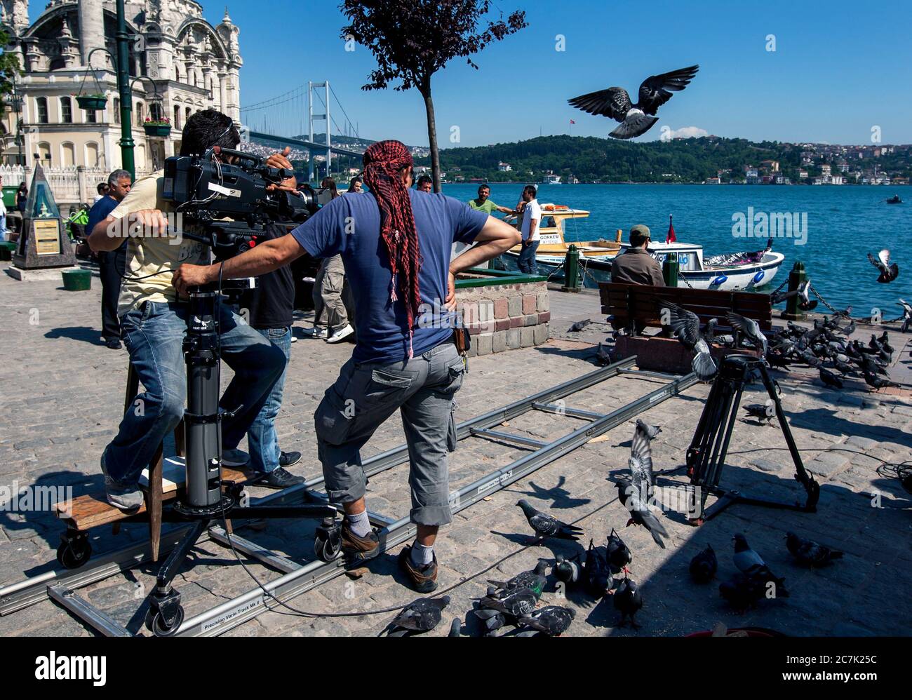 A cameraman films a scene of a man feeding the pigeons adjacent to the ...