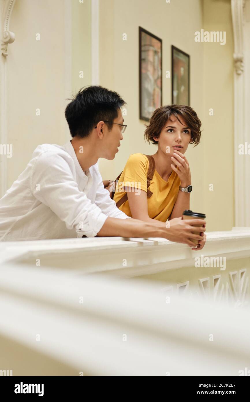 Two young international students thoughtfully talking at break in ...