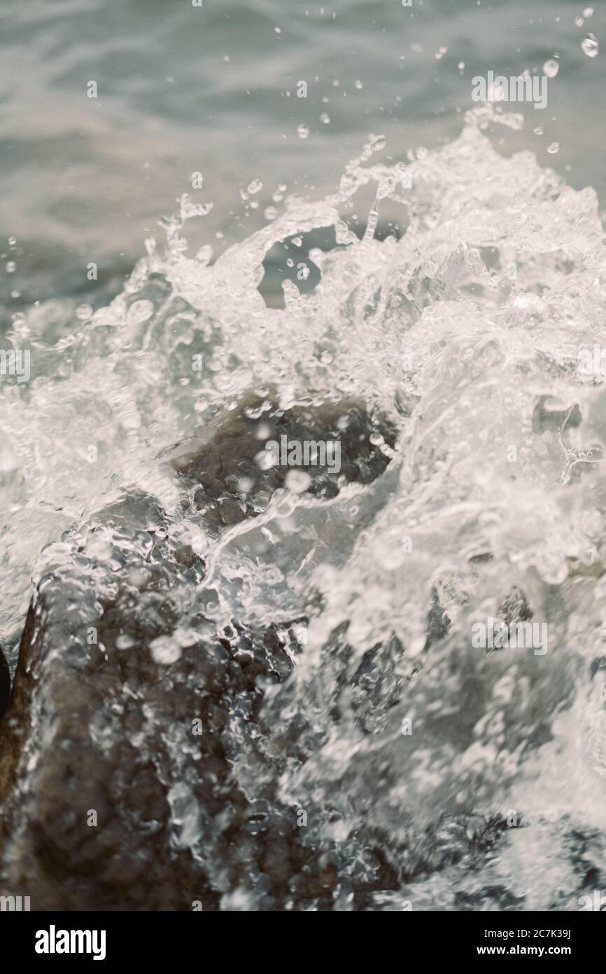 Closeup of a rock in a sea with water splashing on it with a blurry ...