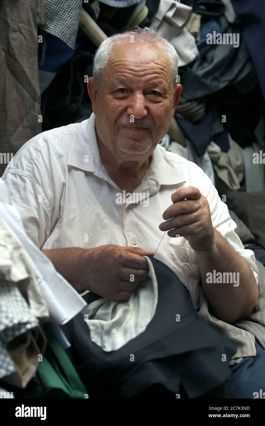A tailor using a needle and thread repairs a suit in his shop within ...