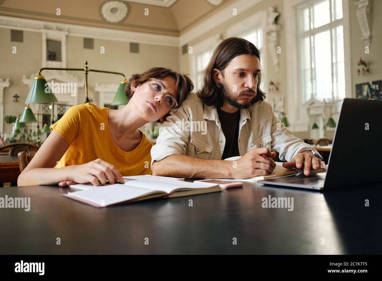 Two young students tiredly working on study project with laptop in ...
