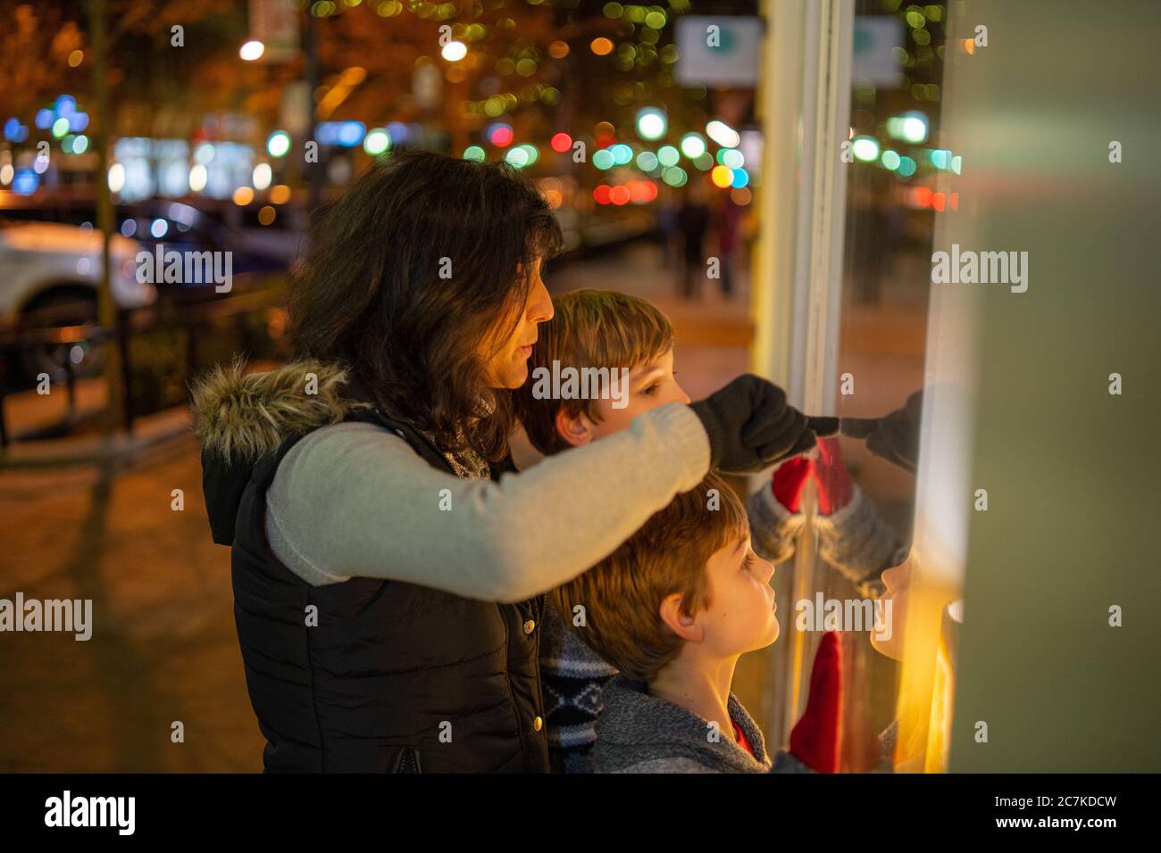 Mother and her two sons standing in front of a window of the shop and ...