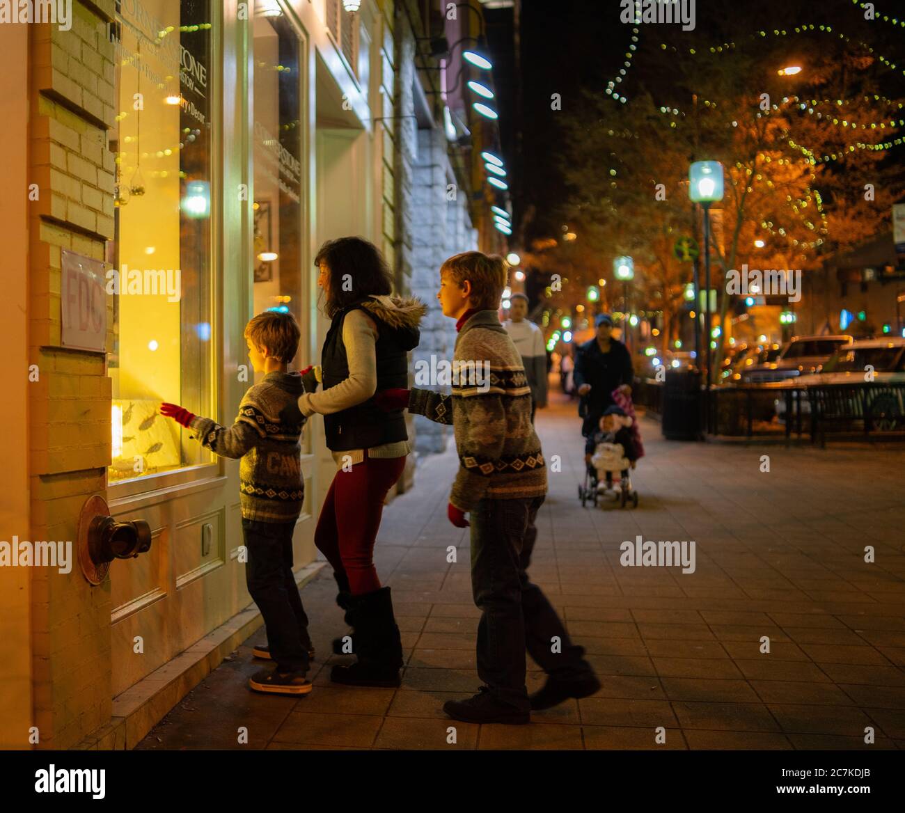 Mother and her two sons standing in front of a window of the shop and ...