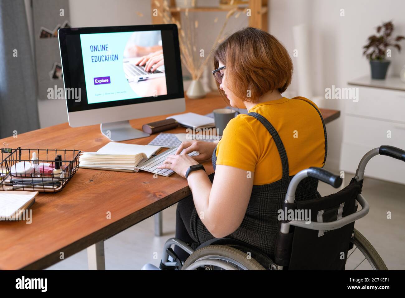 Young female in wheelchair pressing keys on keypad in front of computer ...