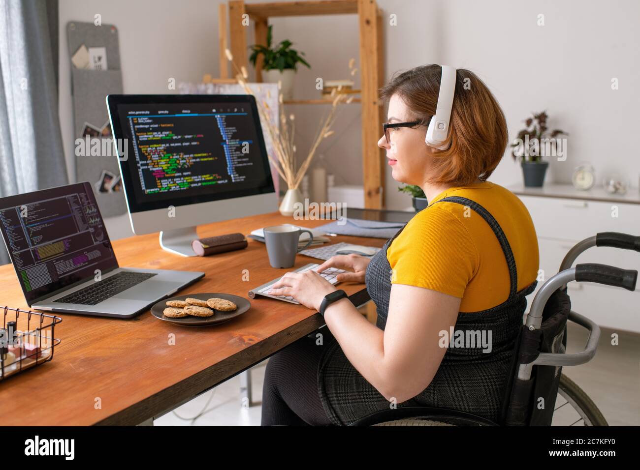 Young pretty female software developer in wheelchair sitting by desk in ...