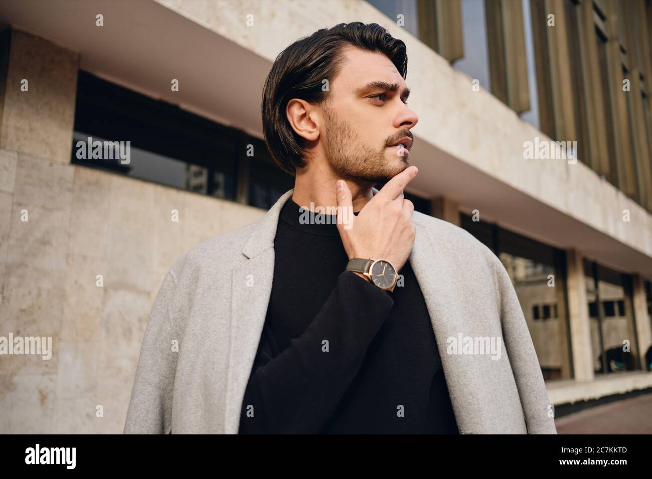 Side view of young wistful man with coat on shoulders thoughtfully ...