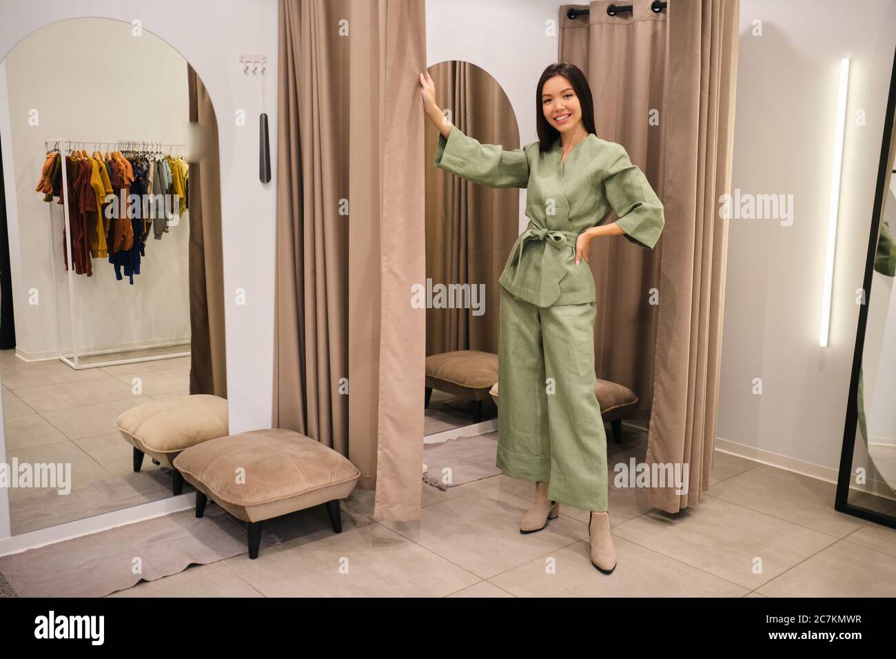 Attractive cheerful Asian girl trying on stylish suit happily looking ...