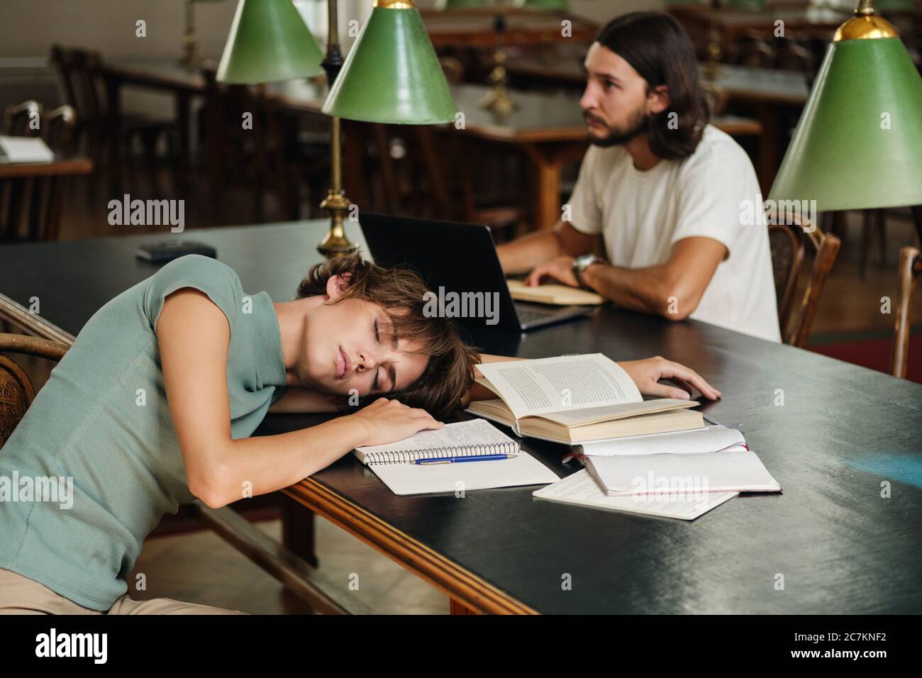 Young tired student sleeping on desk with books during study in library ...