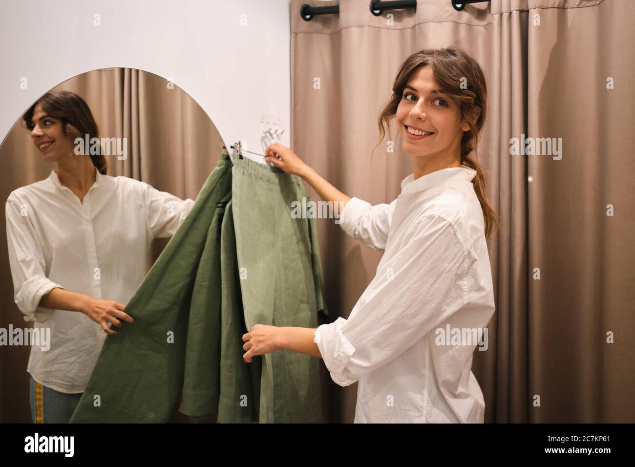 Attractive fashion consultant happily putting clothes in dressing room ...