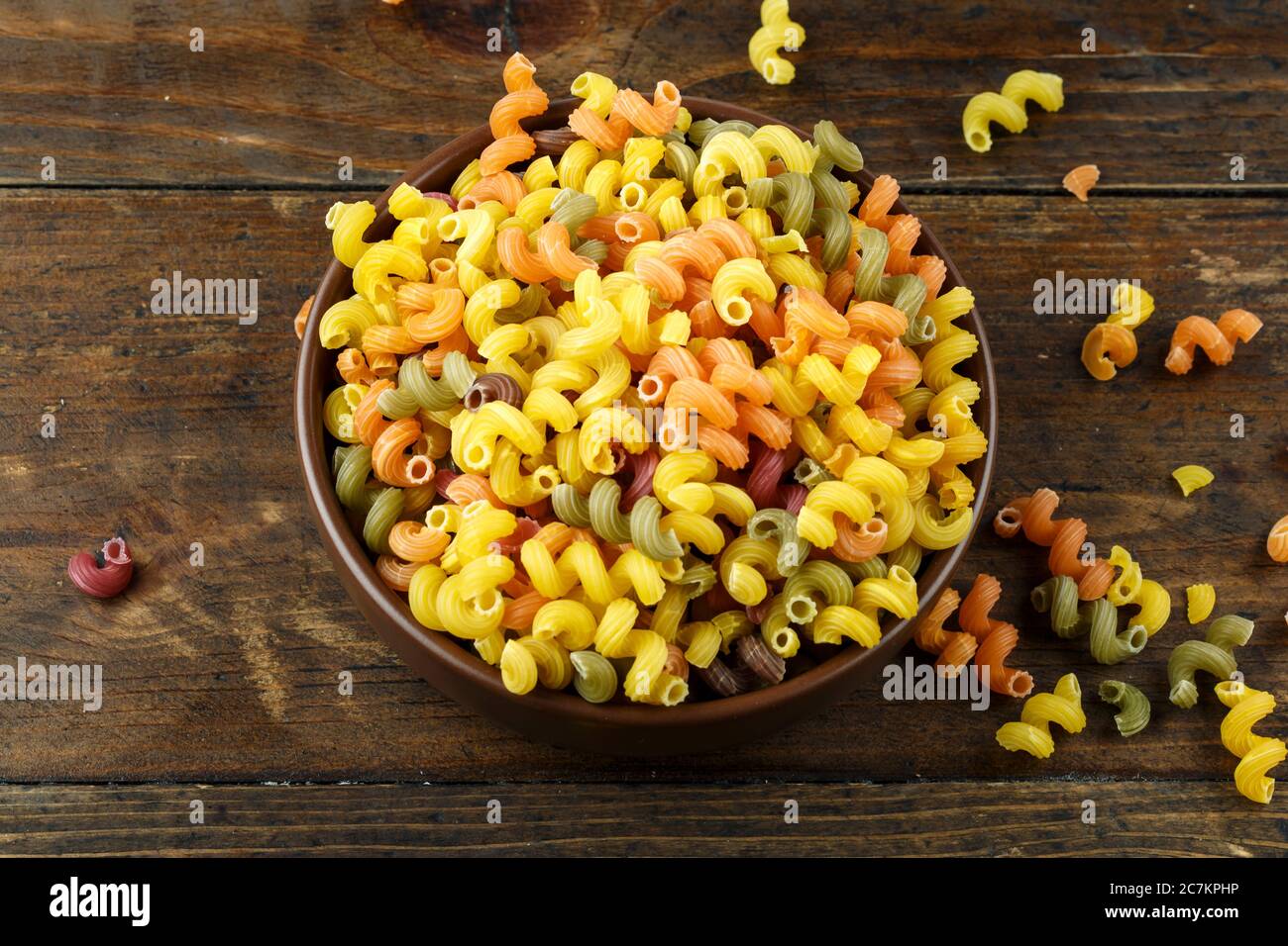 uncooked multi colored pasta in a plate on a wooden background. space ...