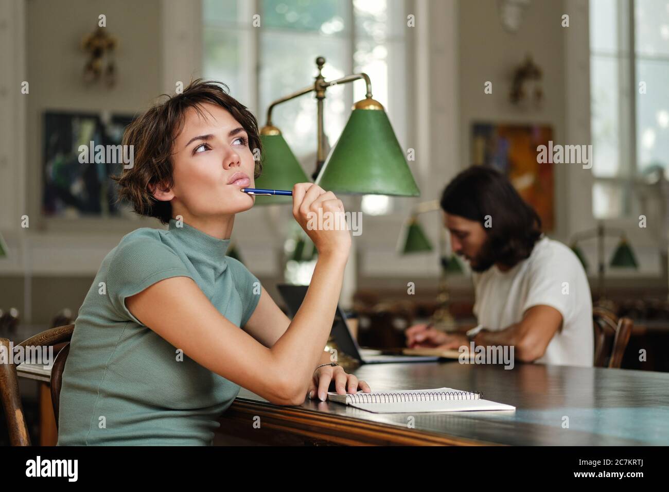Young thoughtful female student thinking about study project in library ...