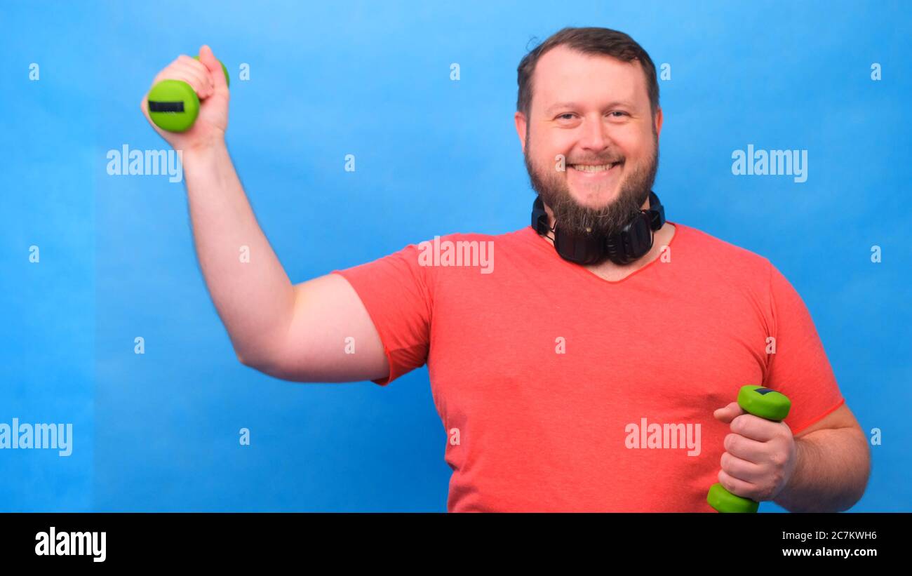 Funny fat man freaky in a wig and a pink t-shirt with dumbbells doing ...