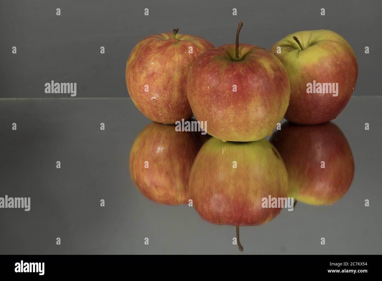Three red apples on mirroring table on mirror gray background with ...