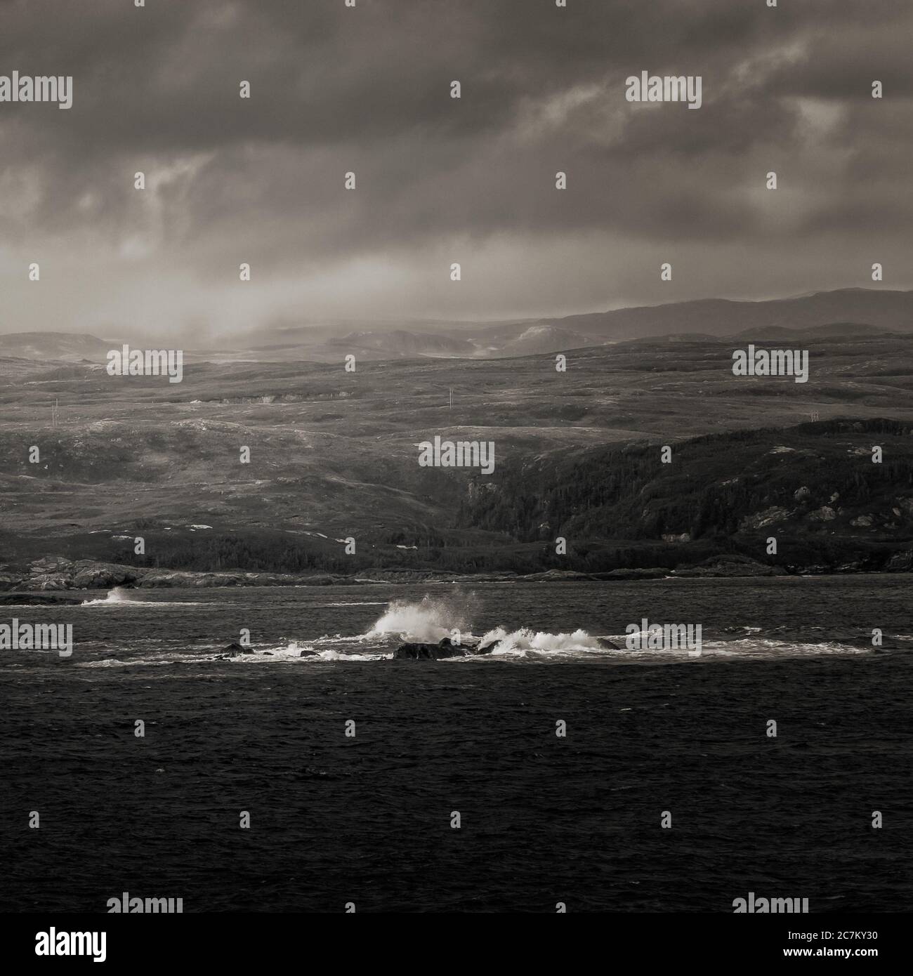 Grayscale shot of a deep ocean and a mountain range on a stormy day ...