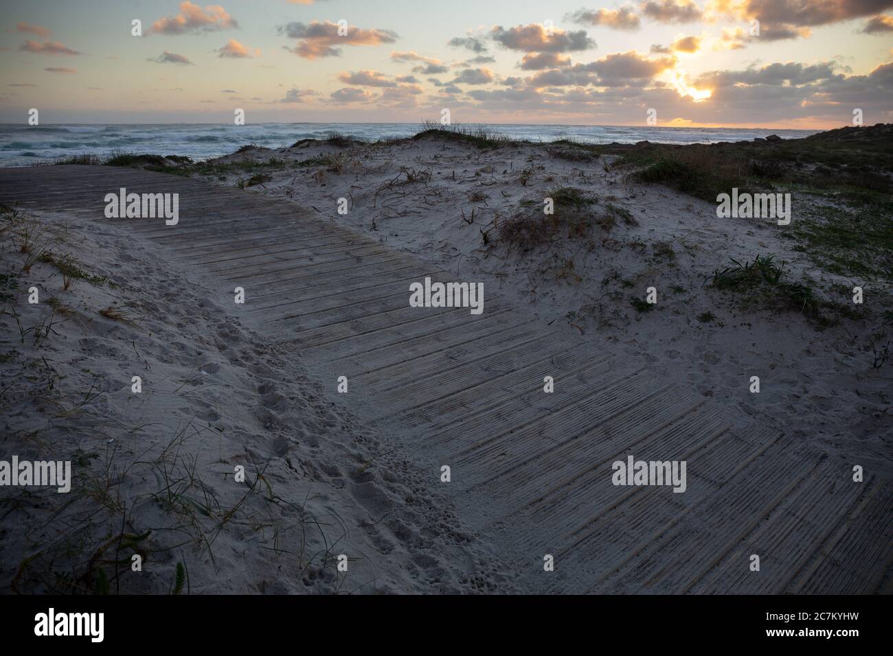 Wide shot of a wooden pathway to the beach in the sand with grass ...
