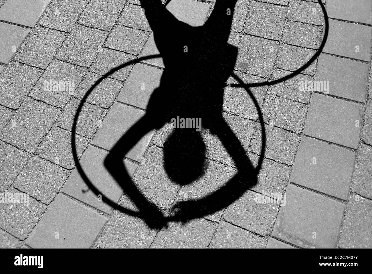 High angle shot of the shadow of a child on a brick pavement doing hula ...