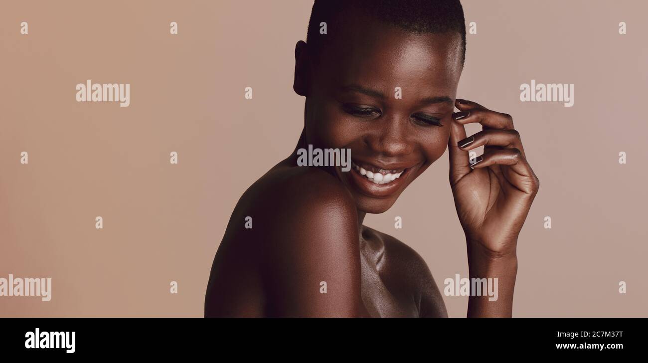 African woman with buzz cut hairstyle looking down and smiling. Female fashion model smiling ...