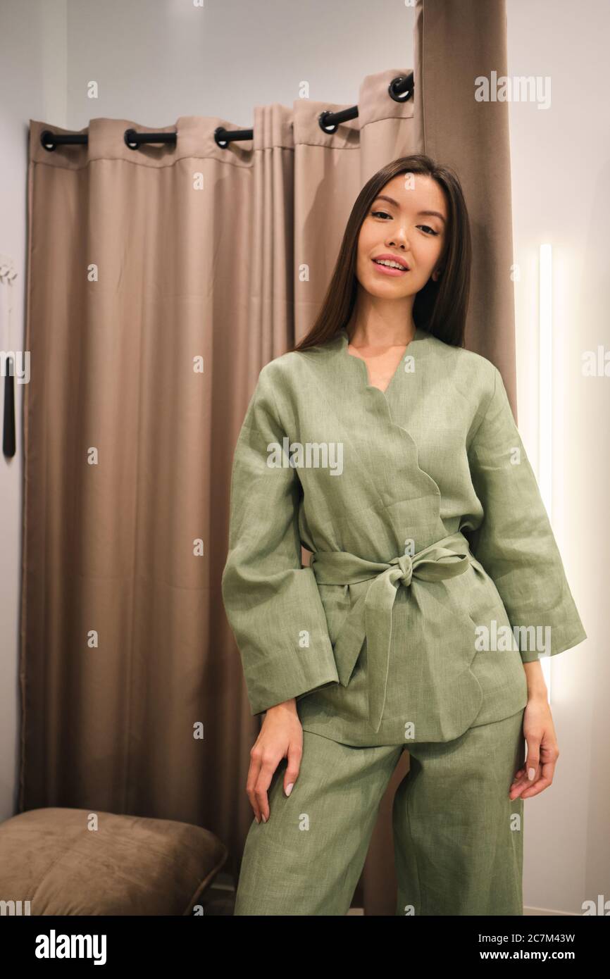 Beautiful smiling Asian girl trying on stylish suit intently looking in ...