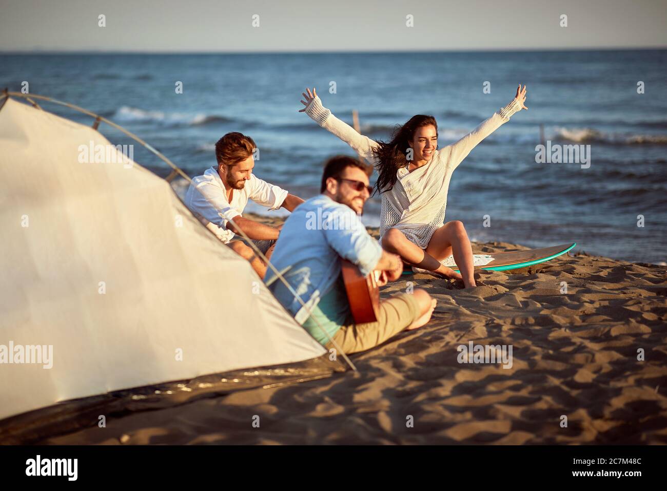 group of friends singing at the beach, enjoying sunset, smiling ...