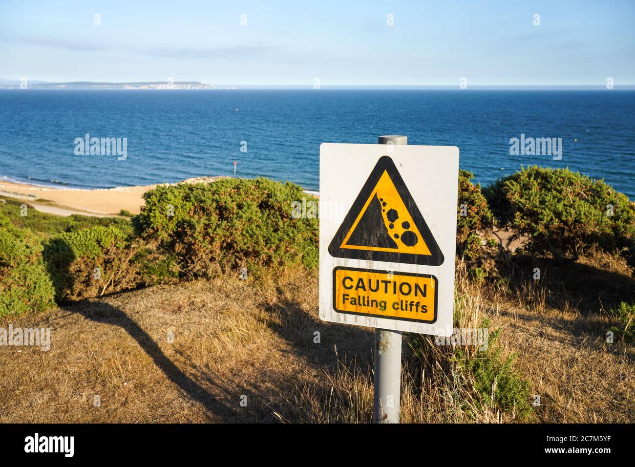 Caution falling cliffs sign on the cliff edge overlooking the sea to ...