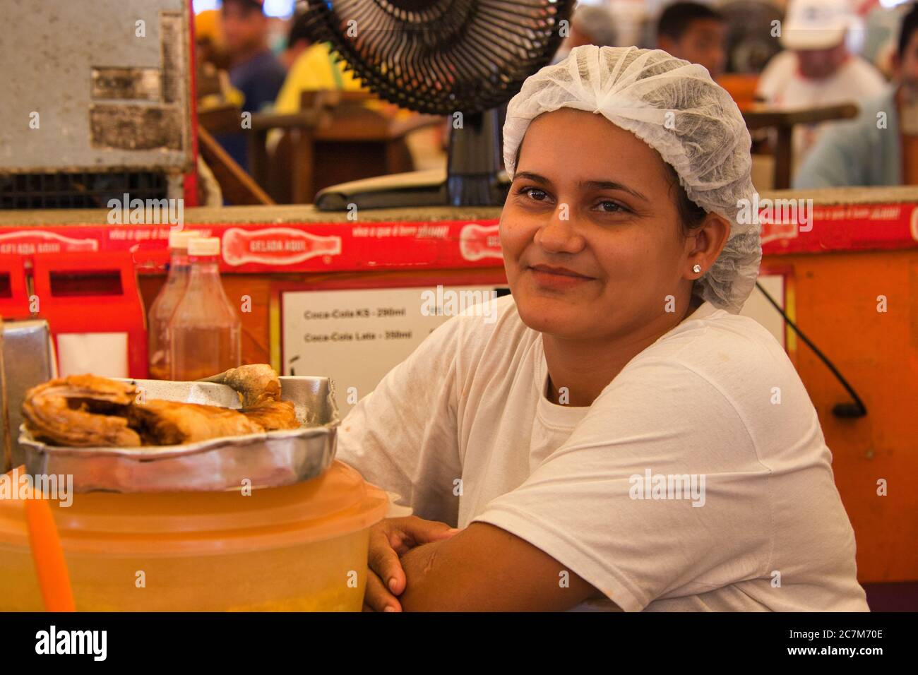 A lady at a food stall stops to look at the camera, in the market at ...