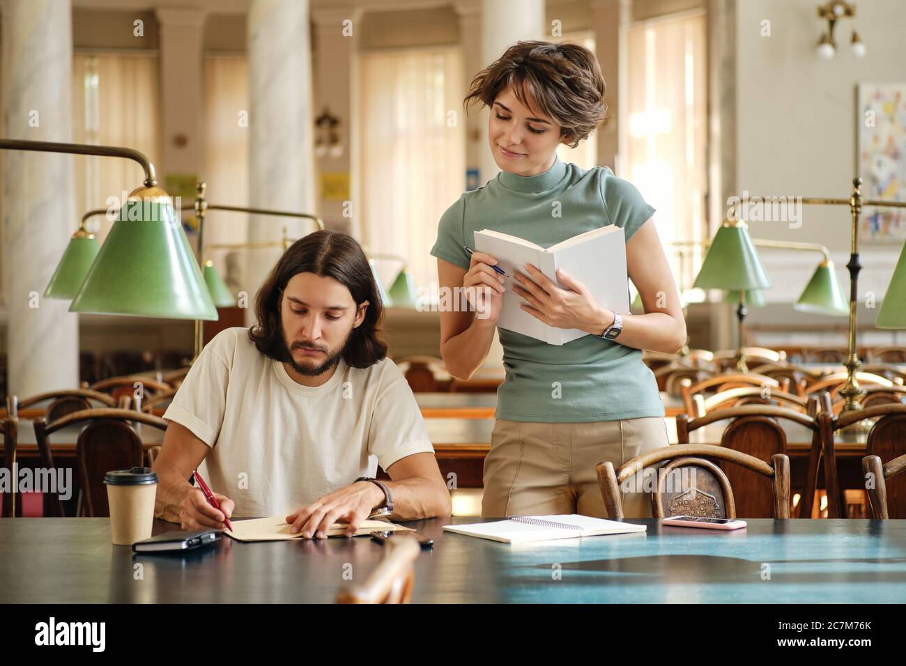 Attractive female tutor with book explaining to young student new theme ...