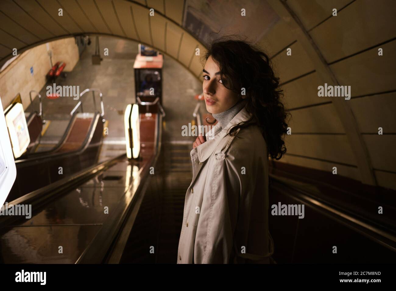 Beautiful girl in trench coat dreamily looking in camera from back on ...