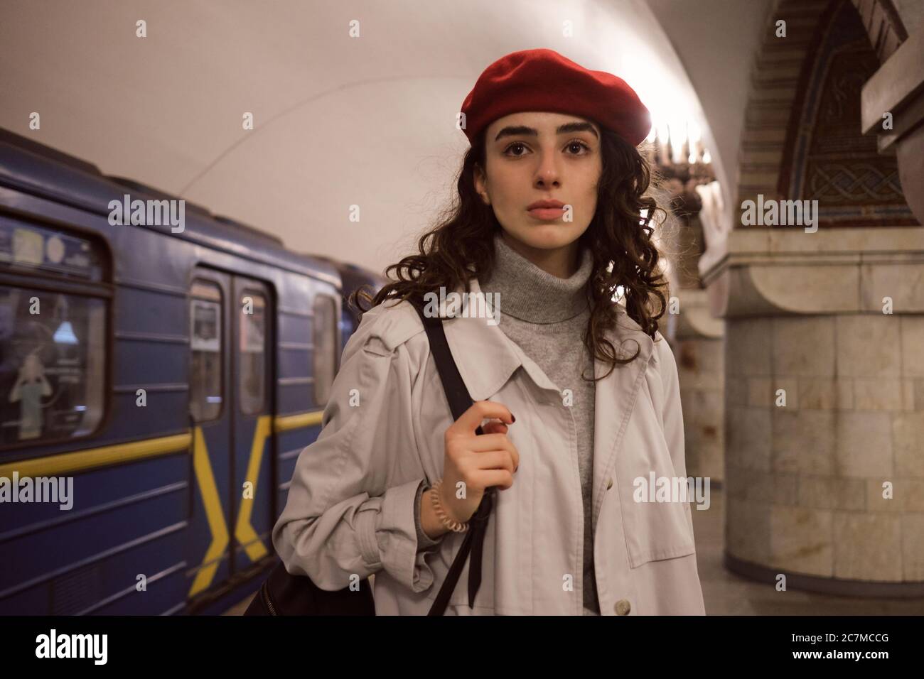 Gorgeous girl in trench coat and red beret thoughtfully waiting train ...