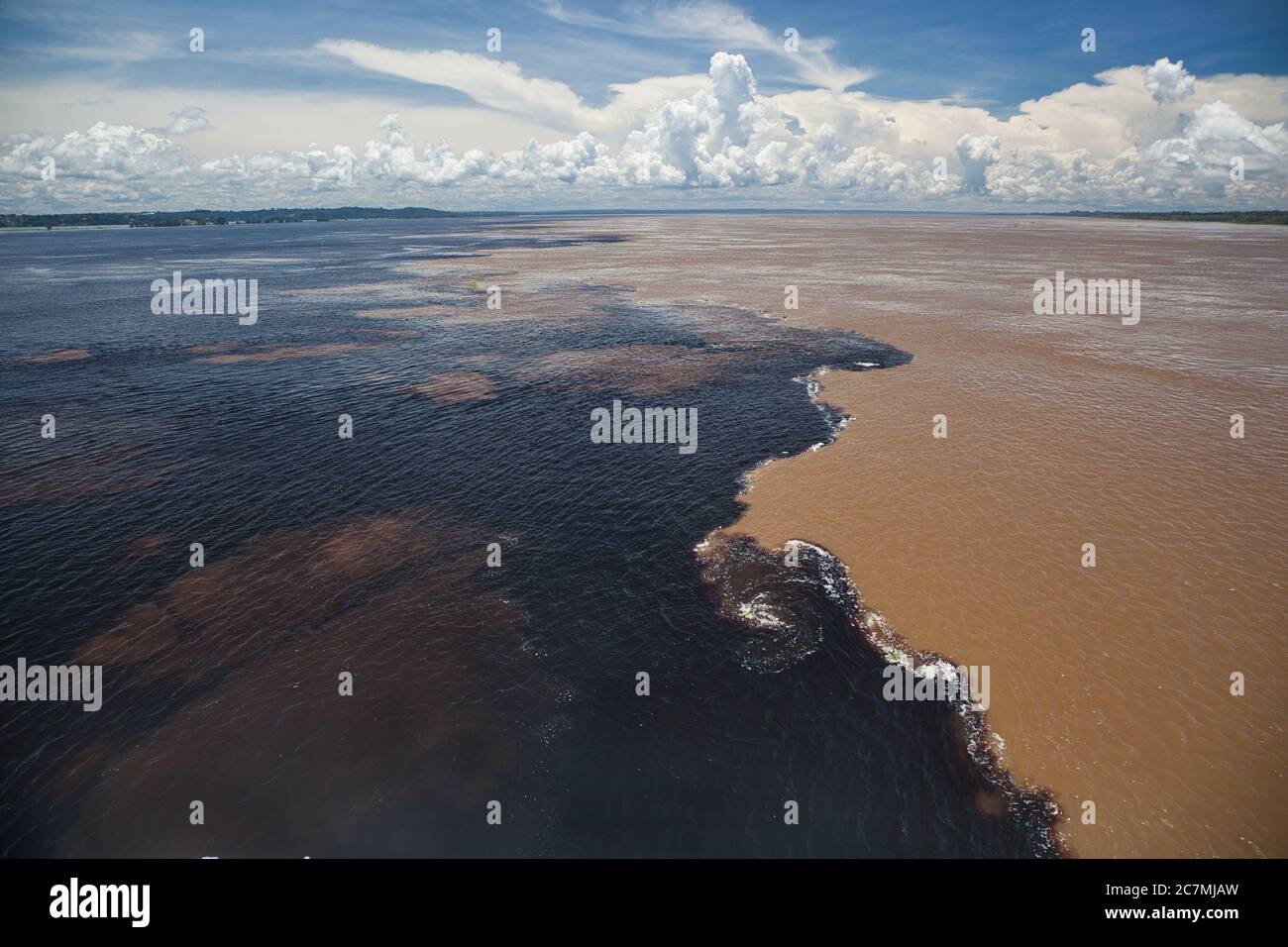 The Meeting of the Waters at the confluence between the dark Rio Negro river and the sandy ...