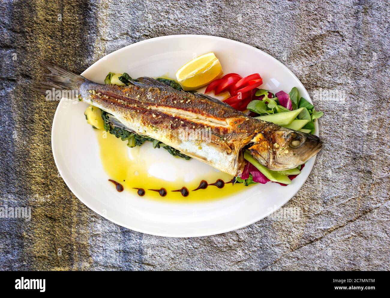 fried fish with fresh herbs, lemon and vegetables on white plate on a ...