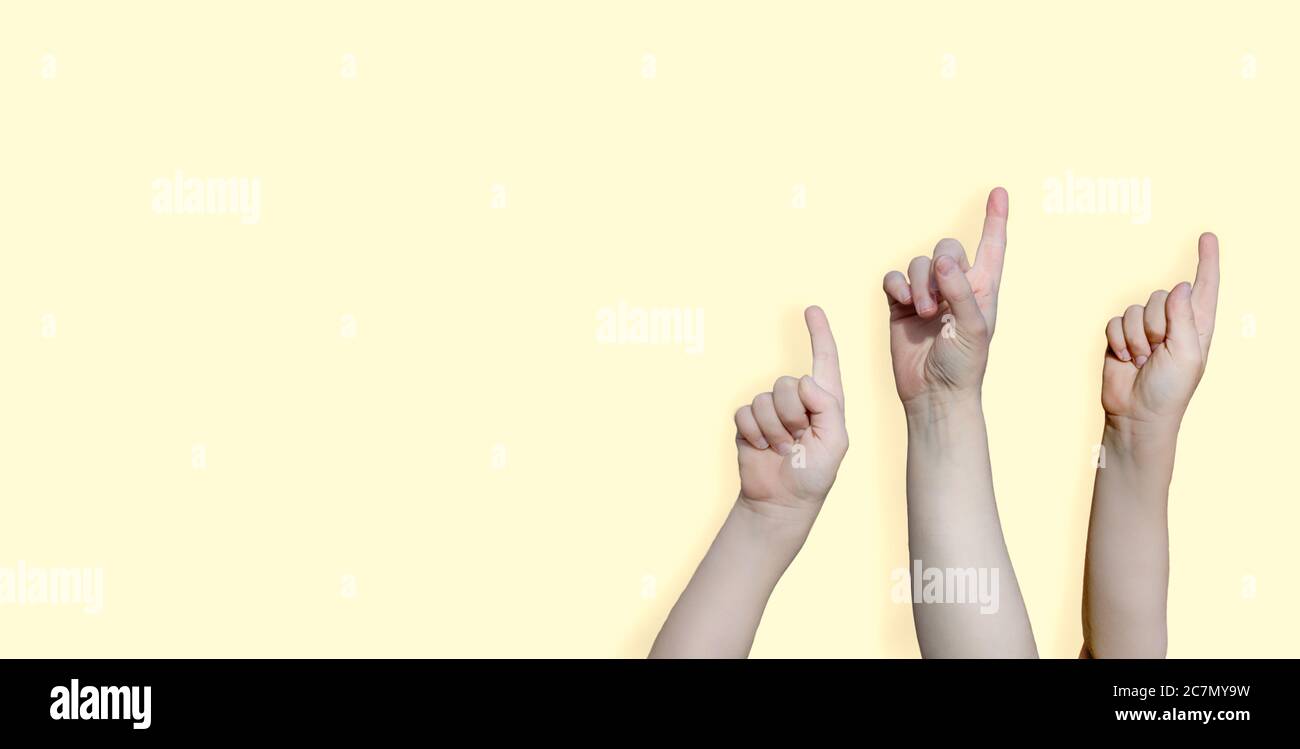 Children hands pointing up on a light yellow background, copy space for ...