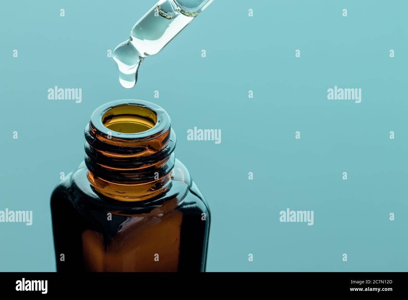A drop of essential oil falling from a pipette into a bottle on a blue ...