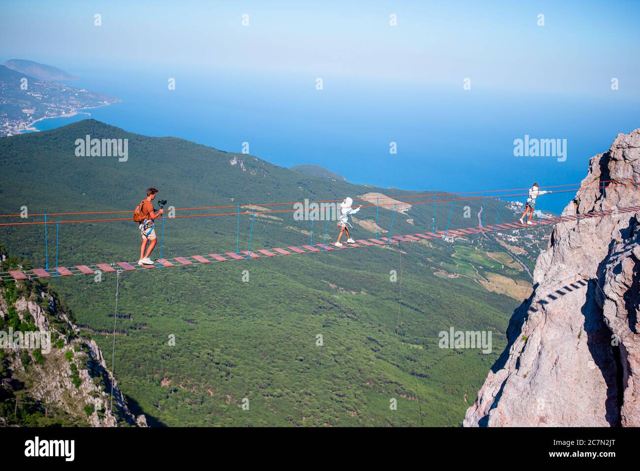 Family crossing the chasm on the rope bridge. Black sea background ...