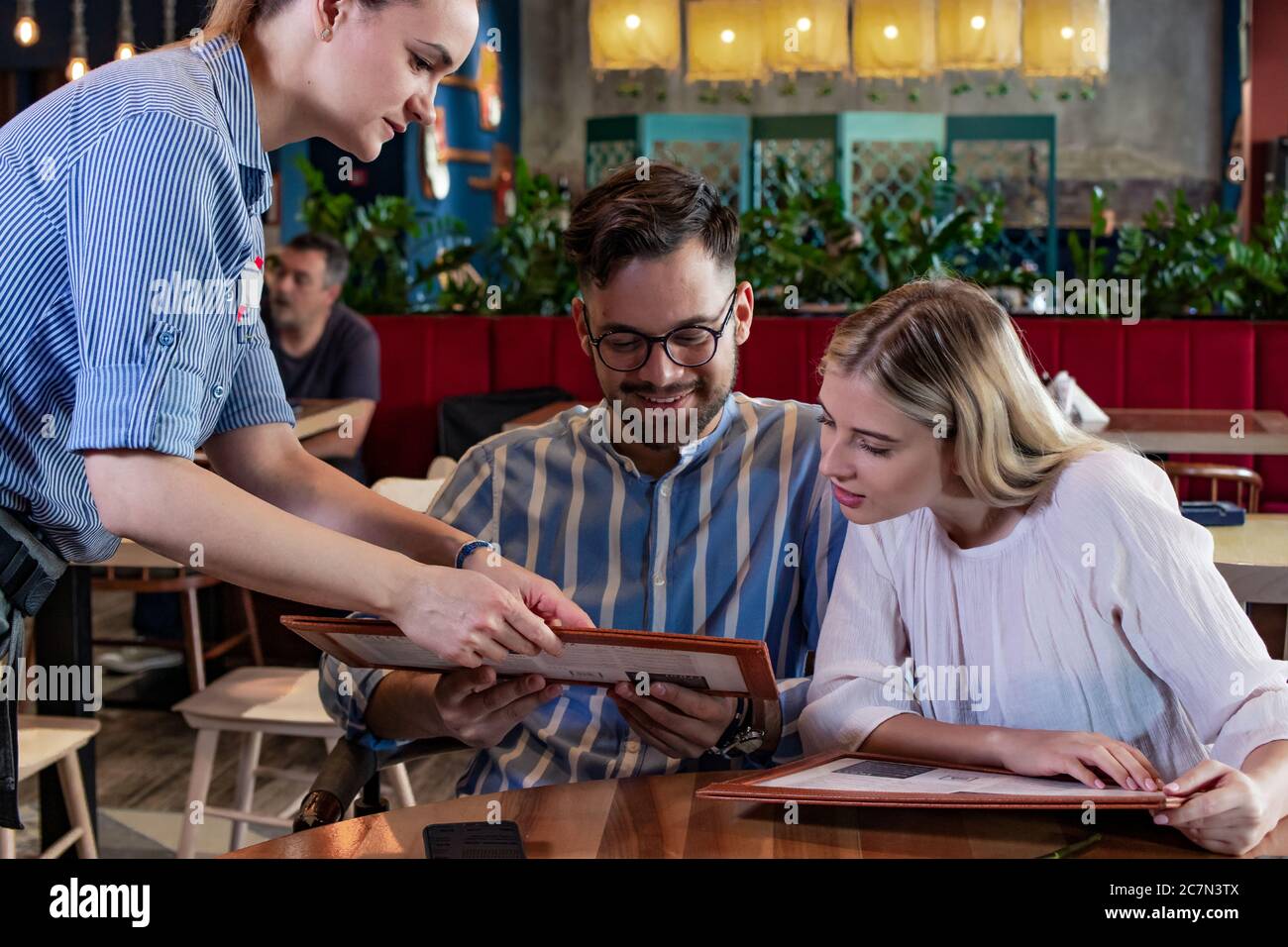 Happy young romantic couple ordering, speaking with a waitress at ...