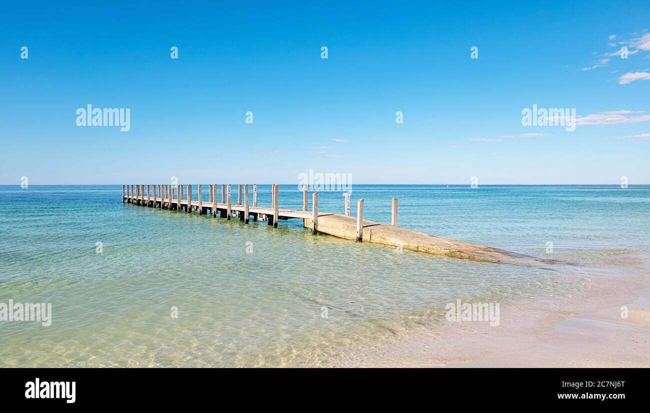 An old wooden boat ramp extends into a turquoise ocean on a sunny day ...