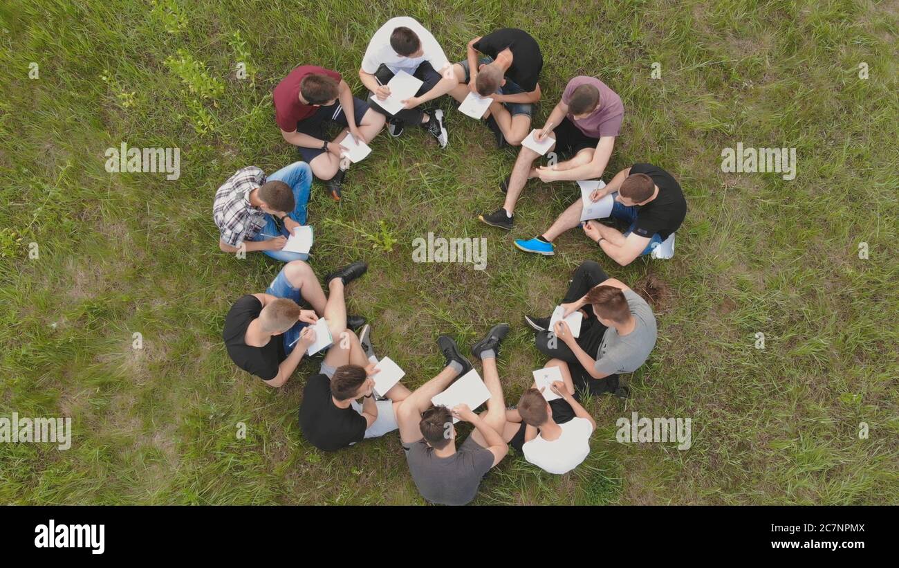 Teamwork concept. A group of high school students sit on the grass in a ...