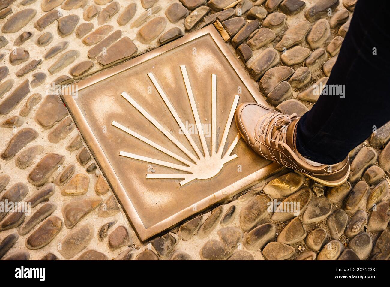 Male foot stepping on a brown tile with a scallop shell symbol in a ...