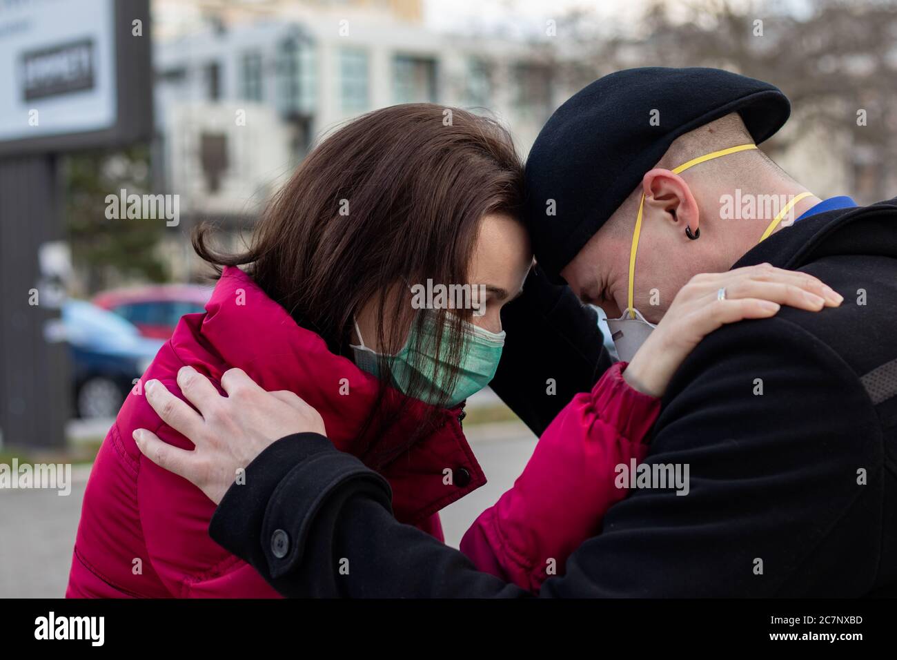 Male and a female hugging on the street while wearing surgical masks to ...