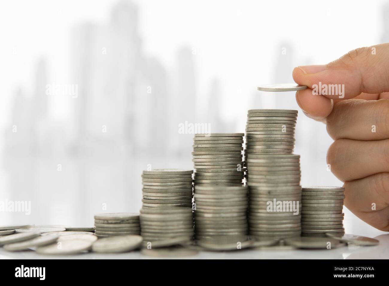 Hand putting coin on coins stack with city in background. Savings ...
