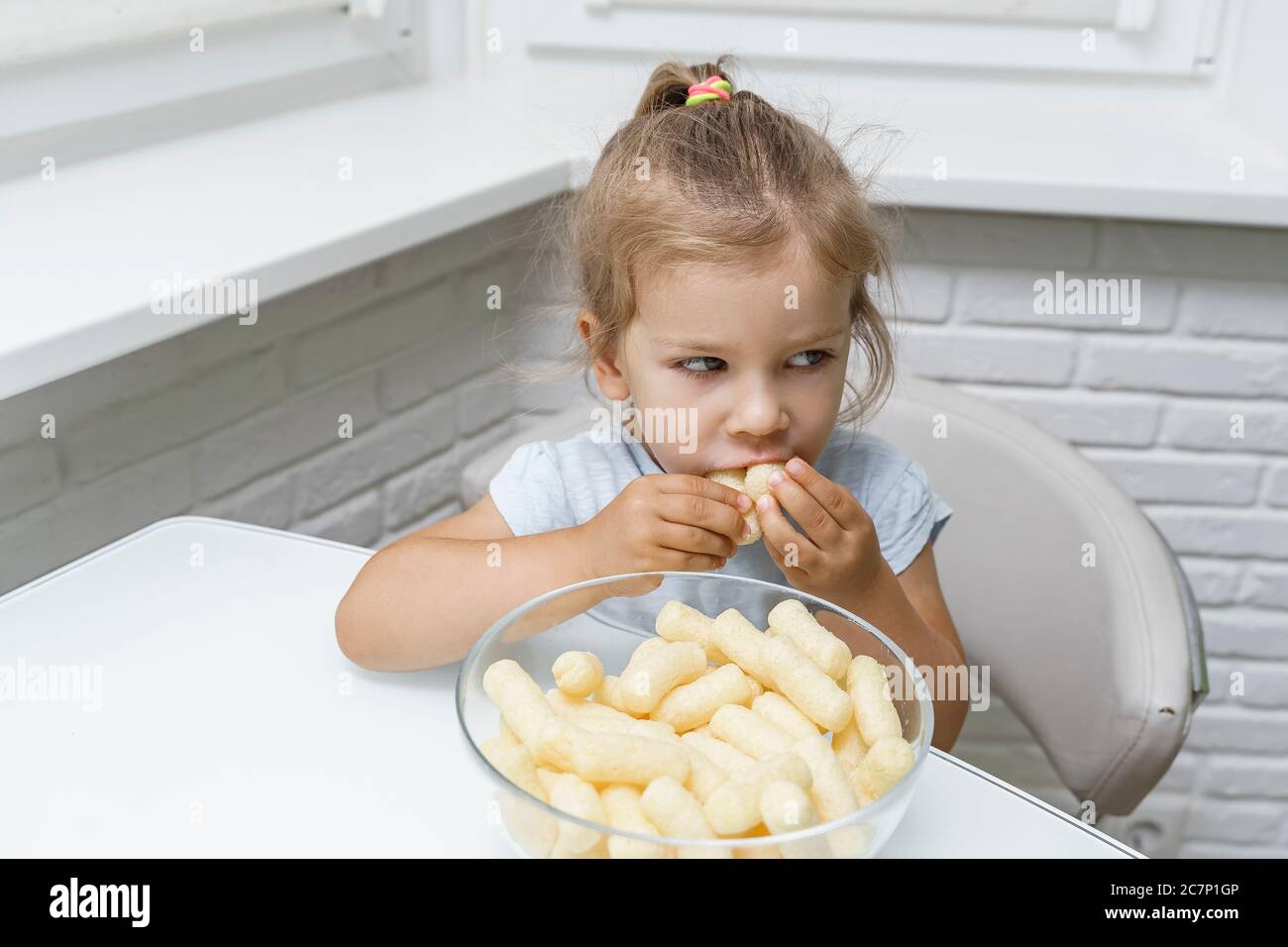 cute little girl puts lots of corn sticks in her mouth and looks at the ...