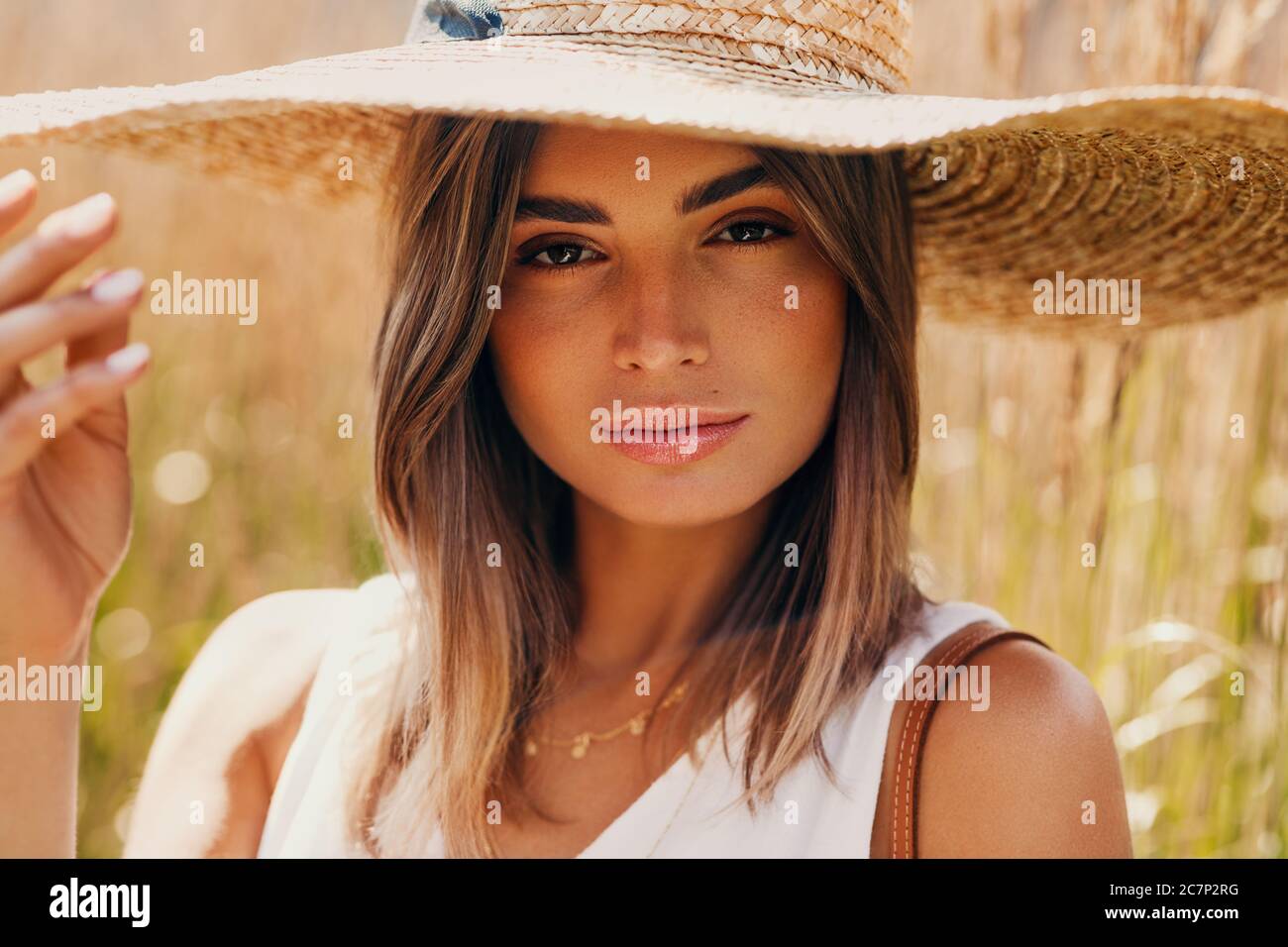 Beautiful woman in straw hat posing on a field and looking at camera ...