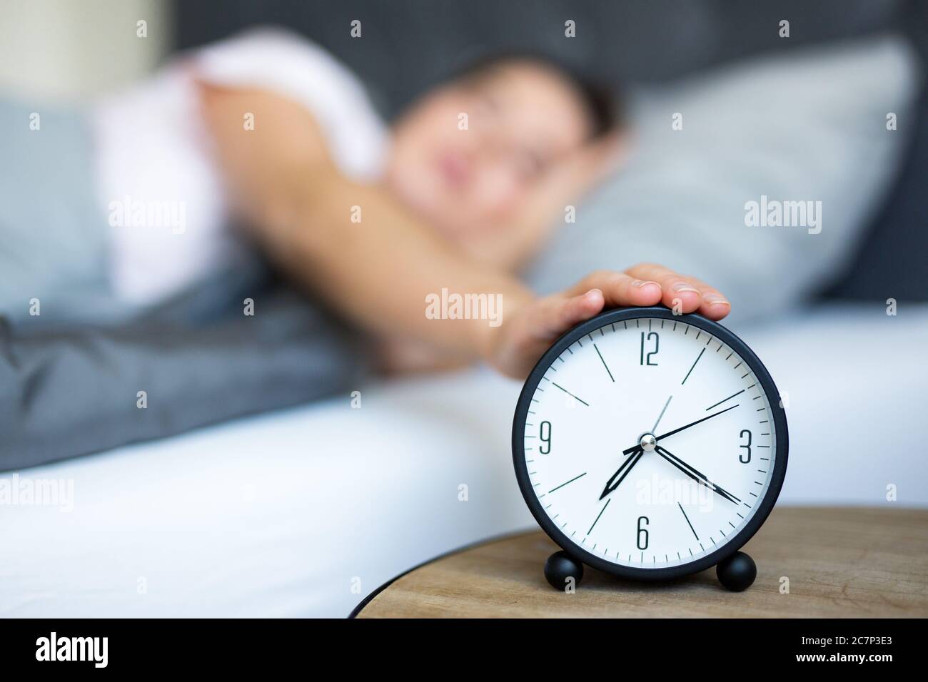 morning concept - young sleepy woman turning off alarm clock in bedroom ...