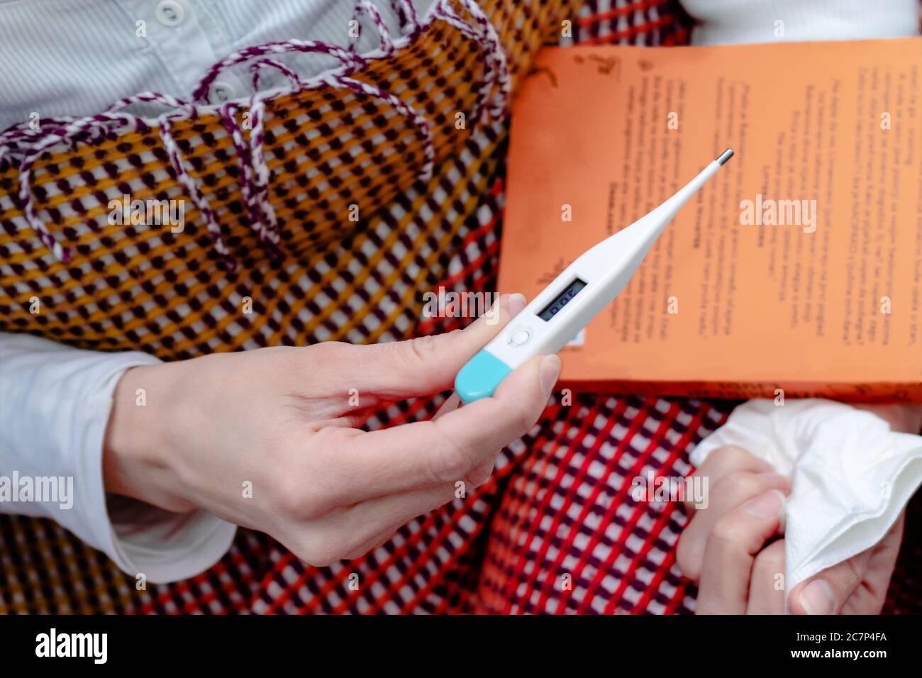 Female holding a book covered with a blanket and a thermometer showing ...